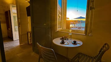 Quarto com mesa redonda, duas cadeiras, janela com vista para a paisagem urbana e porta que dá para outro cômodo.