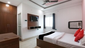 Quarto com cama, televisão fixada na parede, guarda-roupa e janela com cortinas.