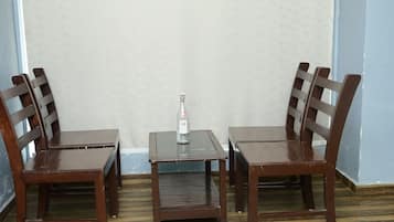 Um quarto com piso de madeira, uma mesa com quatro cadeiras e uma garrafa sobre a mesa.