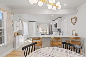 Cozinha moderna com armários brancos, uma ilha central com banquetas e uma luminária pendente.