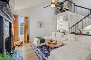 Uma sala de estar ampla com escada moderna, lareira e vista para o exterior.