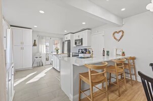 Uma cozinha moderna com armários brancos, uma ilha central com banquetas e uma decoração em formato de coração na parede.