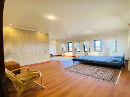 Um quarto espaçoso com uma cama grande, piso de madeira, uma cadeira de fibra natural e vista para o exterior pelas janelas.