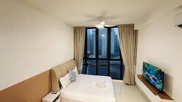 Quarto de hotel com cama, televisão, janela com cortinas e ventoinha no teto.