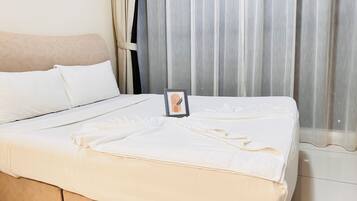 Uma cama bem arrumada com edredom branco e almofadas, um quadro emoldurado sobre a cama e uma janela com cortinas leves.