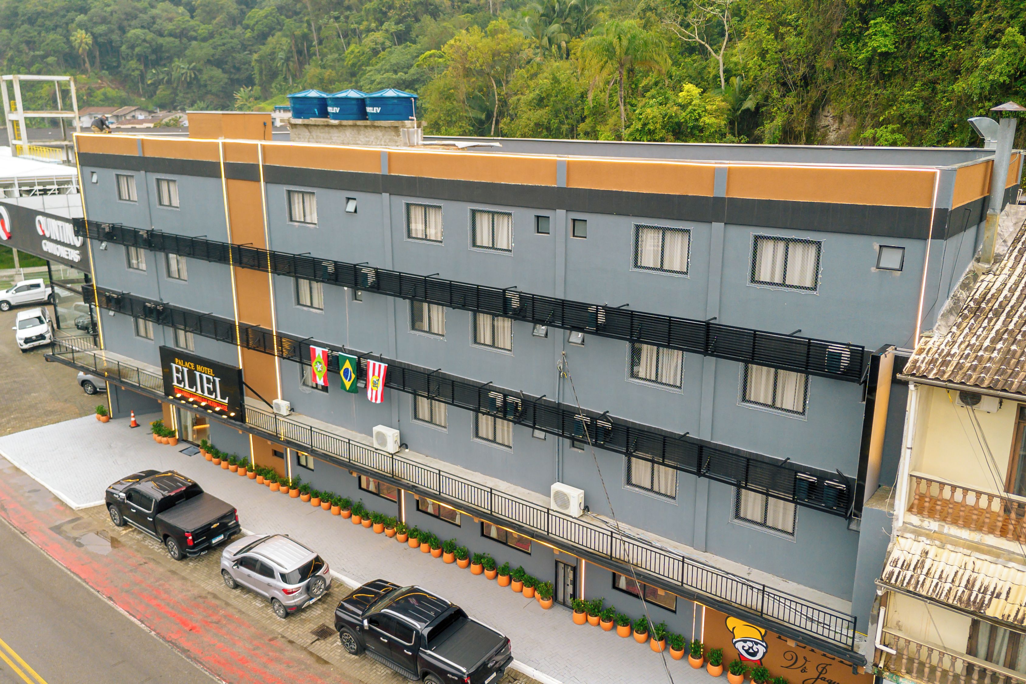 Hotel de vários andares com varandas, área de estacionamento e exibição de bandeiras.
