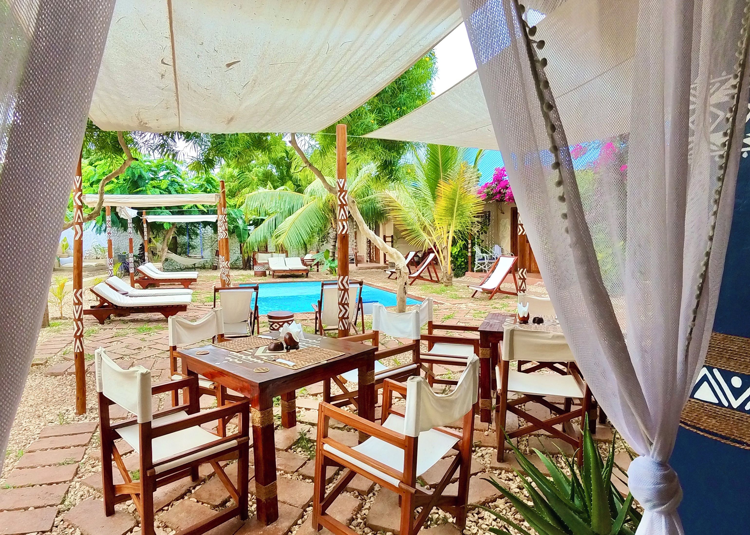 Uma área à beira da piscina com espreguiçadeiras e uma mesa de jantar, cercada por vegetação e uma piscina azul cristalina.