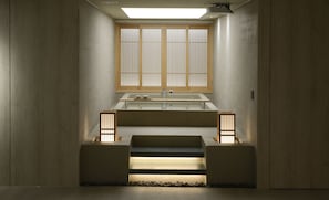 Casa de banho minimalista com lavatório embutido, janela com persianas verticais e um degrau a levar a uma área com pedras.