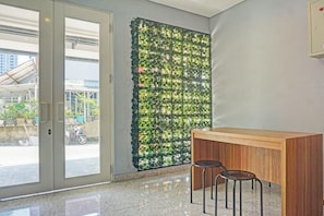 Quarto com porta de vidro que dá para o exterior, balcão de madeira com dois bancos e parede com instalação de folhagem verde.