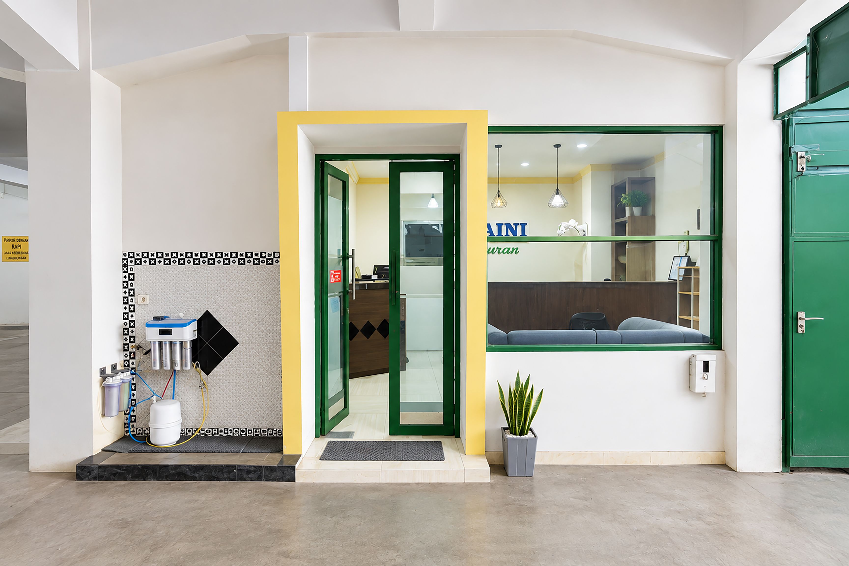 Uma área de recepção com entrada por porta de vidro, balcão de recepção e planta em vaso.