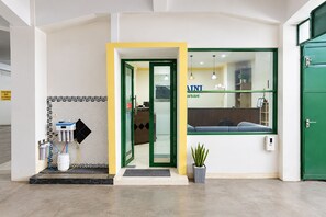 Uma área de recepção com entrada por porta de vidro, balcão de recepção e planta em vaso.