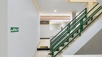 Escada com grades verdes que leva a um patamar com luminária e um objeto emoldurado na parede.