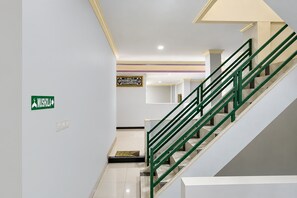 Escada com grades verdes que leva a um patamar com luminária e um objeto emoldurado na parede.