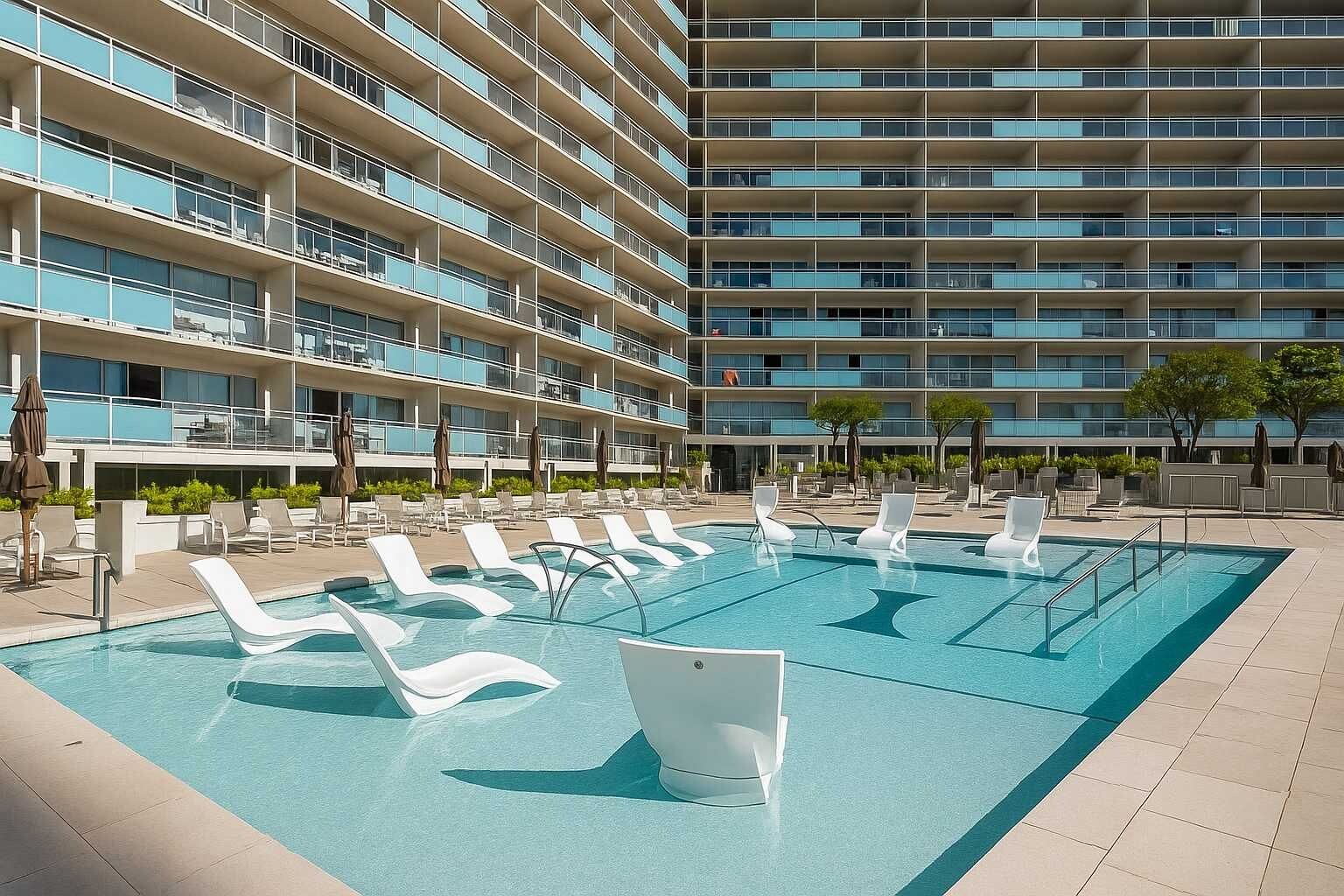 Área de piscina de hotel com várias espreguiçadeiras e um edifício grande ao fundo.