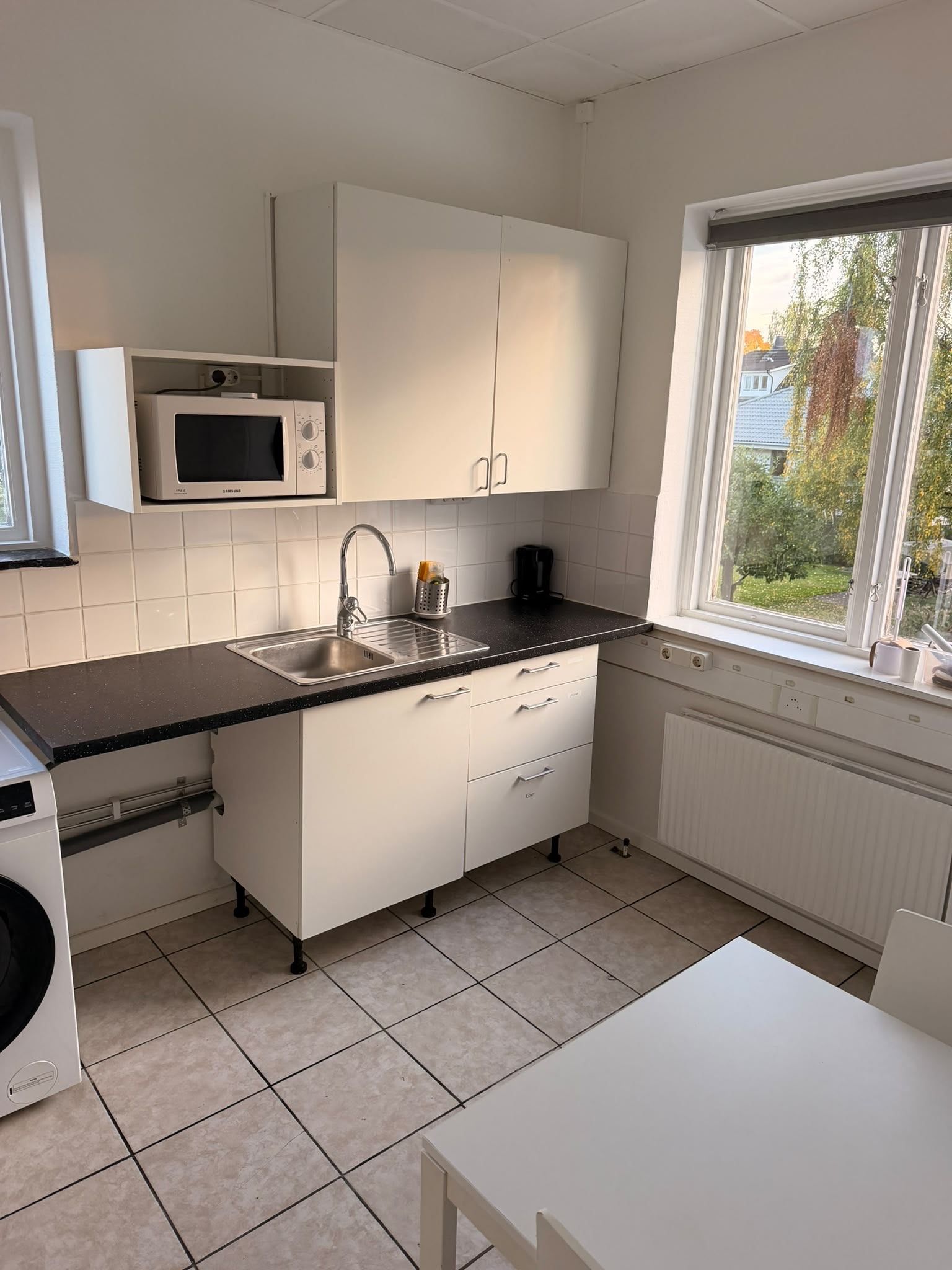 Cozinha moderna com armários brancos, micro-ondas embutido, pia e janela com vista para o exterior.