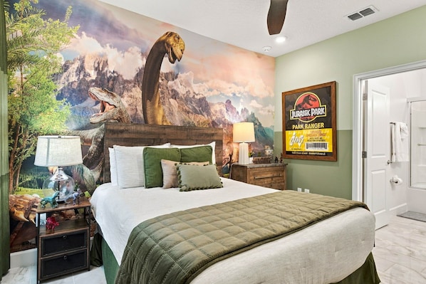 Quarto com um grande mural de dinossauros, uma cama com colcha verde e um cartaz de um guarda florestal.