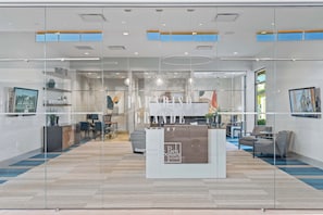 Uma área de recepção moderna com divisória de vidro, balcão de atendimento, espaço para sentar e vista para o interior.