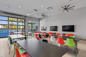 Uma sala de jantar moderna com mesas e cadeiras, janelas amplas, ventiladores de teto e obras de arte nas paredes.