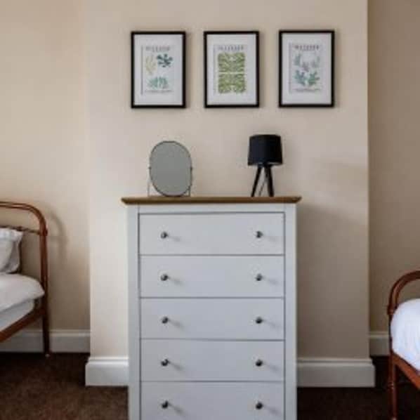 Quarto com cama, penteadeira e três gravuras botânicas emolduradas na parede.
