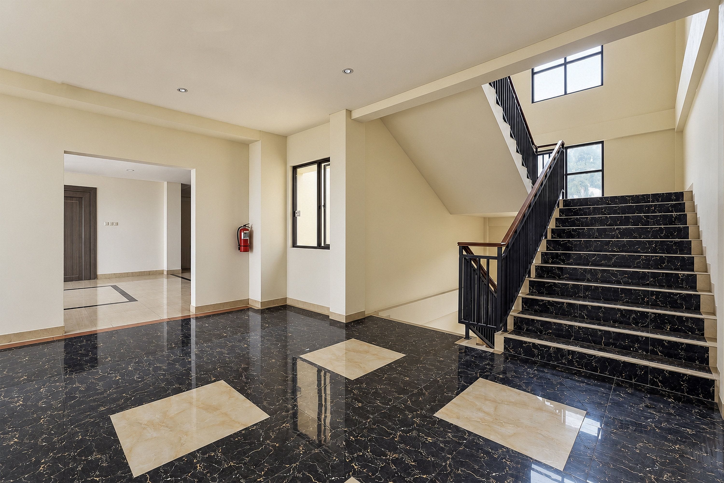 Amplo interior com escadaria de mármore preto, um extintor de incêndio e uma porta que dá para outro cômodo.