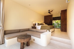 Quarto moderno com sofá, mesa de madeira redonda e cama com vista para o verde.