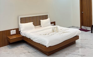 Quarto de hotel moderno, com estrutura de cama de madeira, roupa de cama branca e piso com padrão marmorizado.