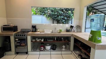 Cozinha compacta com micro-ondas, fogão e pia. Há uma janela com vista para o verde lá fora.