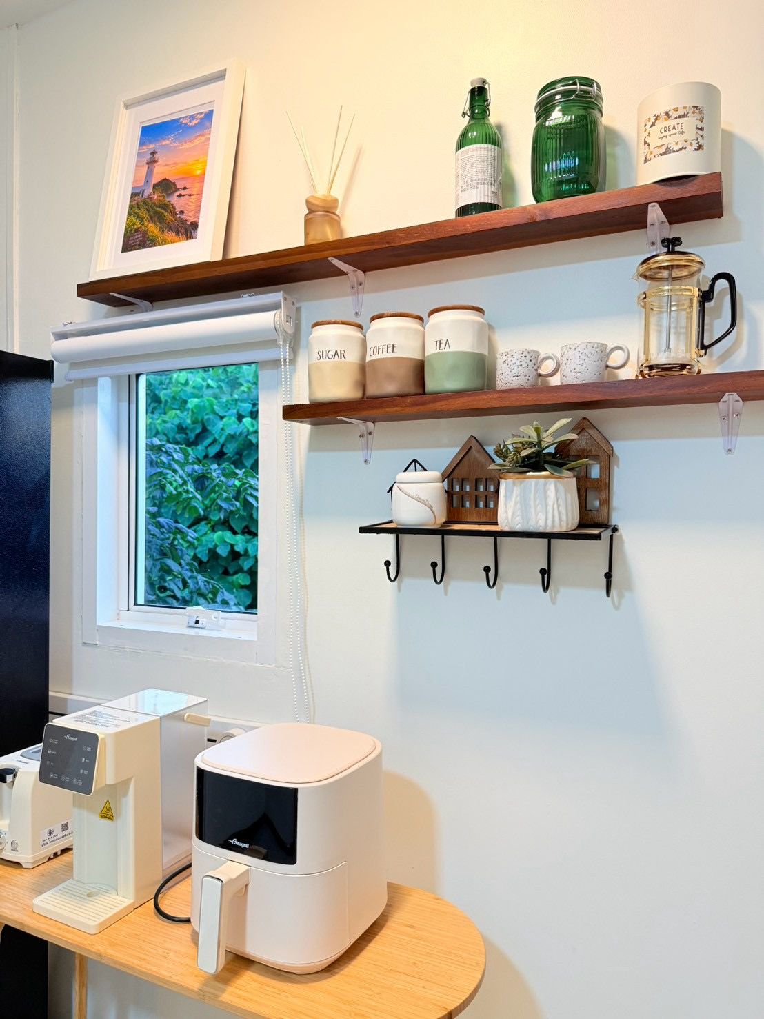 Uma área de cozinha com cafeteira, janela com vista para o verde e prateleiras com utensílios de cozinha e objetos decorativos.