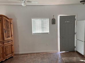 Um quarto com um armário de madeira, uma janela com persianas, uma porta e um ventilador de teto.