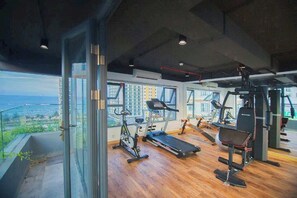 Academia com equipamentos de ginástica, amplas janelas e vista para a cidade.