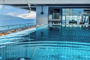 Piscina infinita moderna com vista desimpedida para o mar e montanhas, toldo e área de estar com vista.