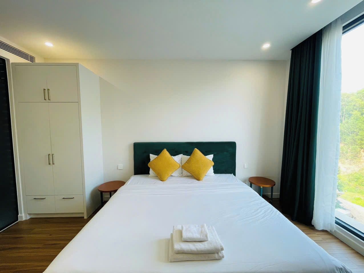 Quarto de hotel com cama, duas mesas de cabeceira, guarda-roupa e janela com cortinas.