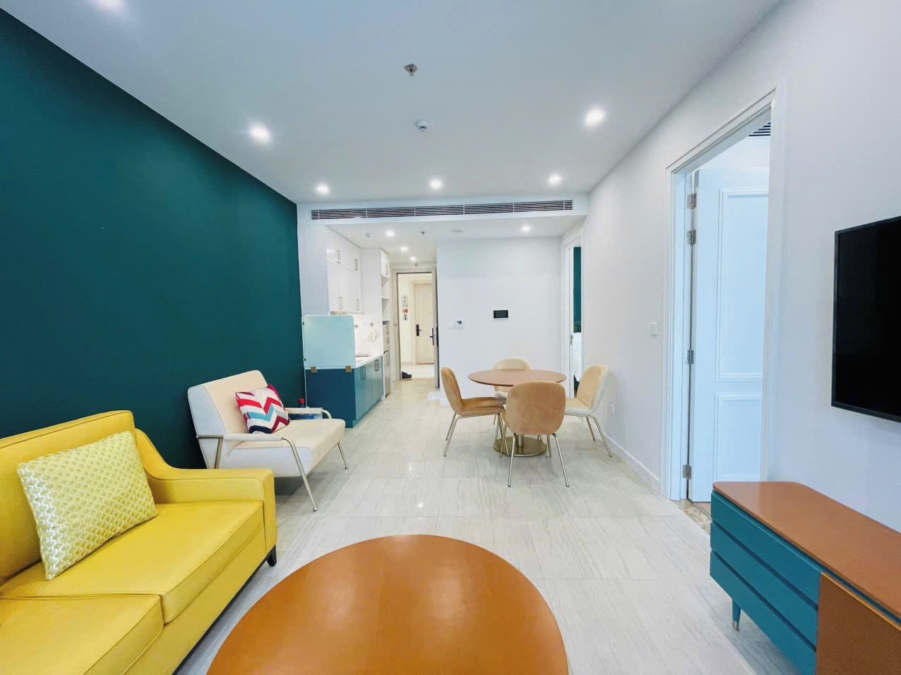 Uma sala de estar moderna com um sofá amarelo, uma mesa de centro redonda e uma área de refeições com mesa e cadeiras.