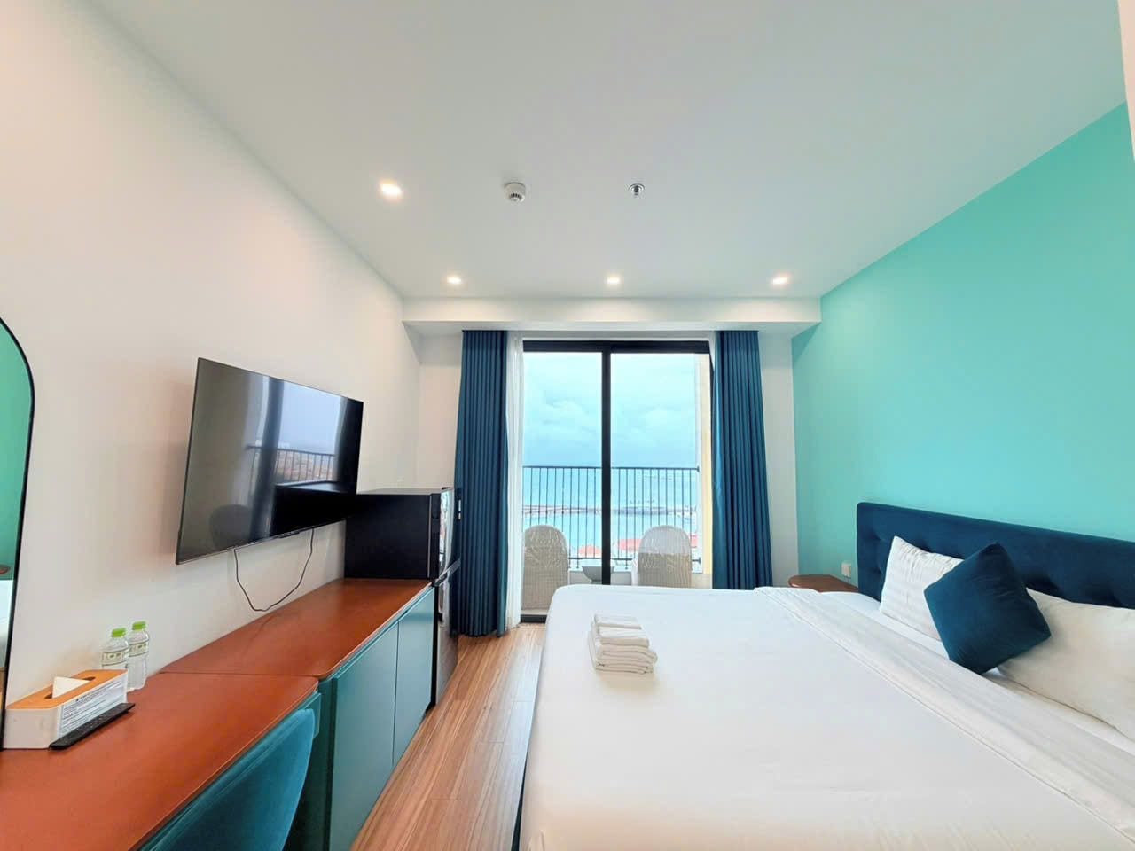 Quarto de hotel com cama, escrivaninha, televisão e varanda com vista.
