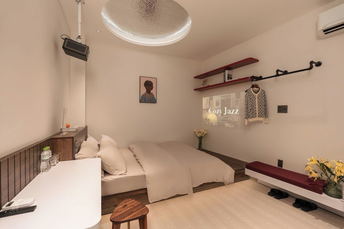 Quarto moderno com cama, mesa de cabeceira e um pequeno espaço de trabalho.