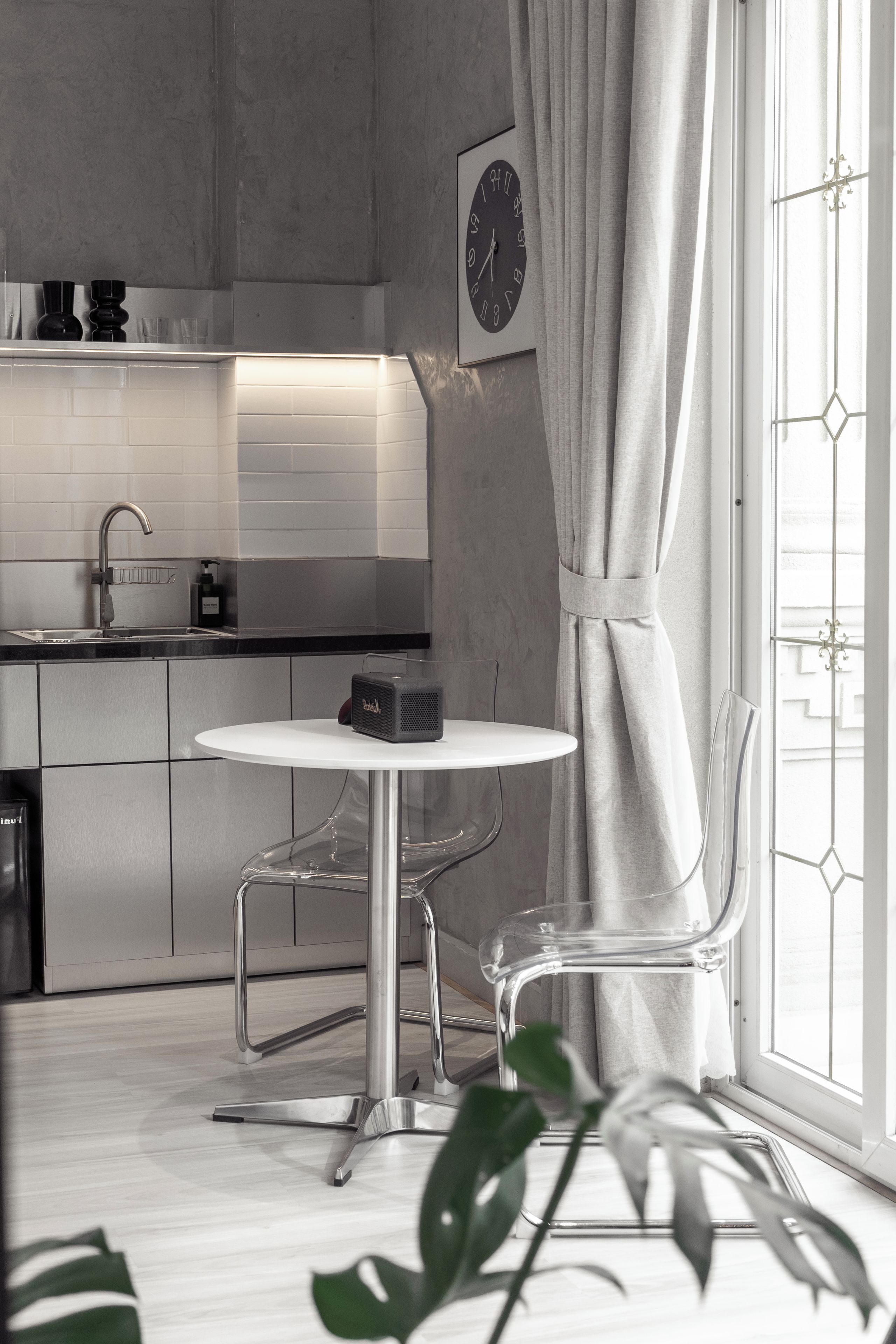 Cozinha moderna com mesa redonda, cadeiras transparentes, forno embutido e janela com cortinas.
