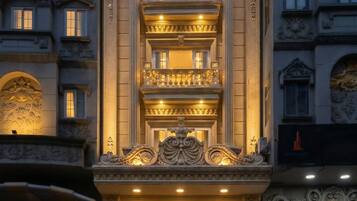 Fachada imponente de um hotel, com arquitetura ornamentada, várias varandas e iluminação cuidadosa.
