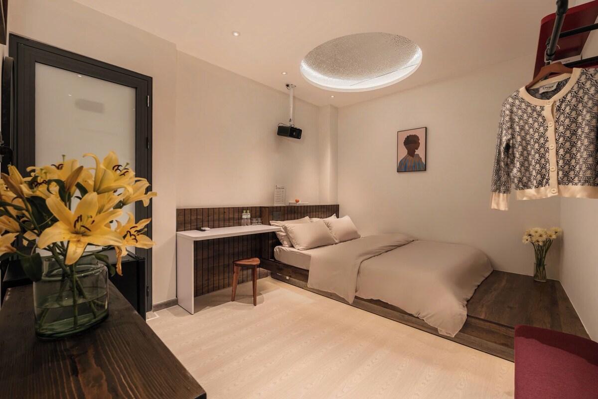 Quarto moderno com cama, mesa de cabeceira e área de trabalho.