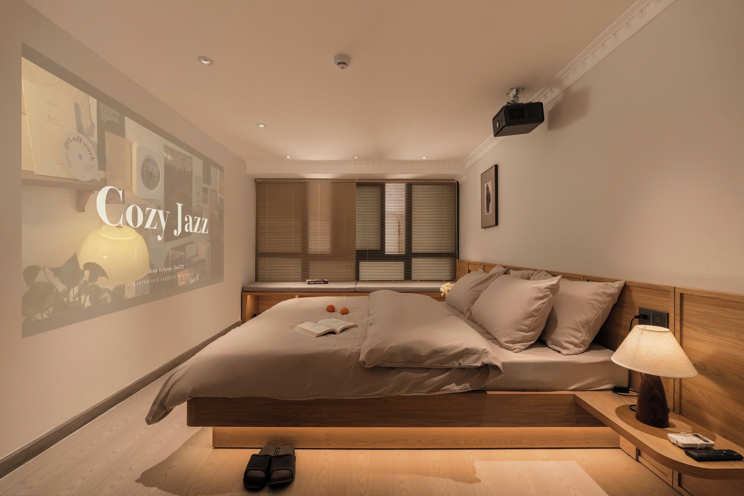 Quarto moderno com cama, tela de projetor exibindo imagem com tema de jazz, mesa de cabeceira com abajur e janela com persianas.