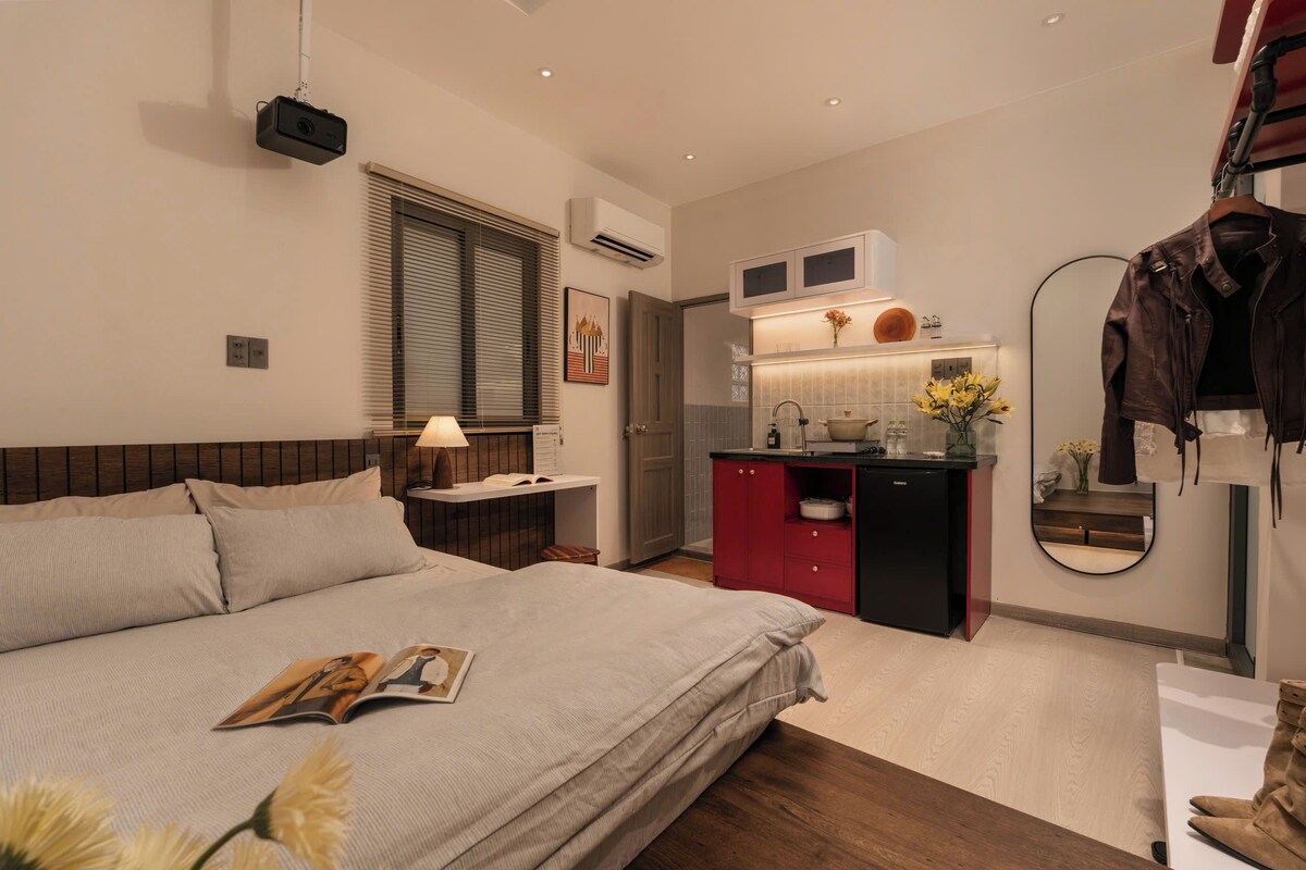 Quarto moderno com cama grande, mesa de cabeceira, abajur e uma revista.