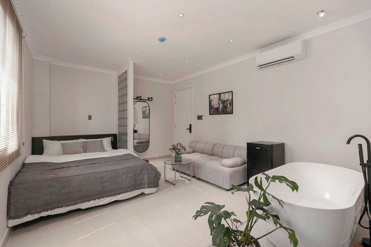 Quarto moderno com cama, sofá, espelho grande, ar-condicionado fixado na parede e banheira.