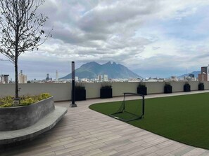 Terraço no telhado com um gol de futebol, uma árvore e vista para uma montanha e o horizonte urbano.