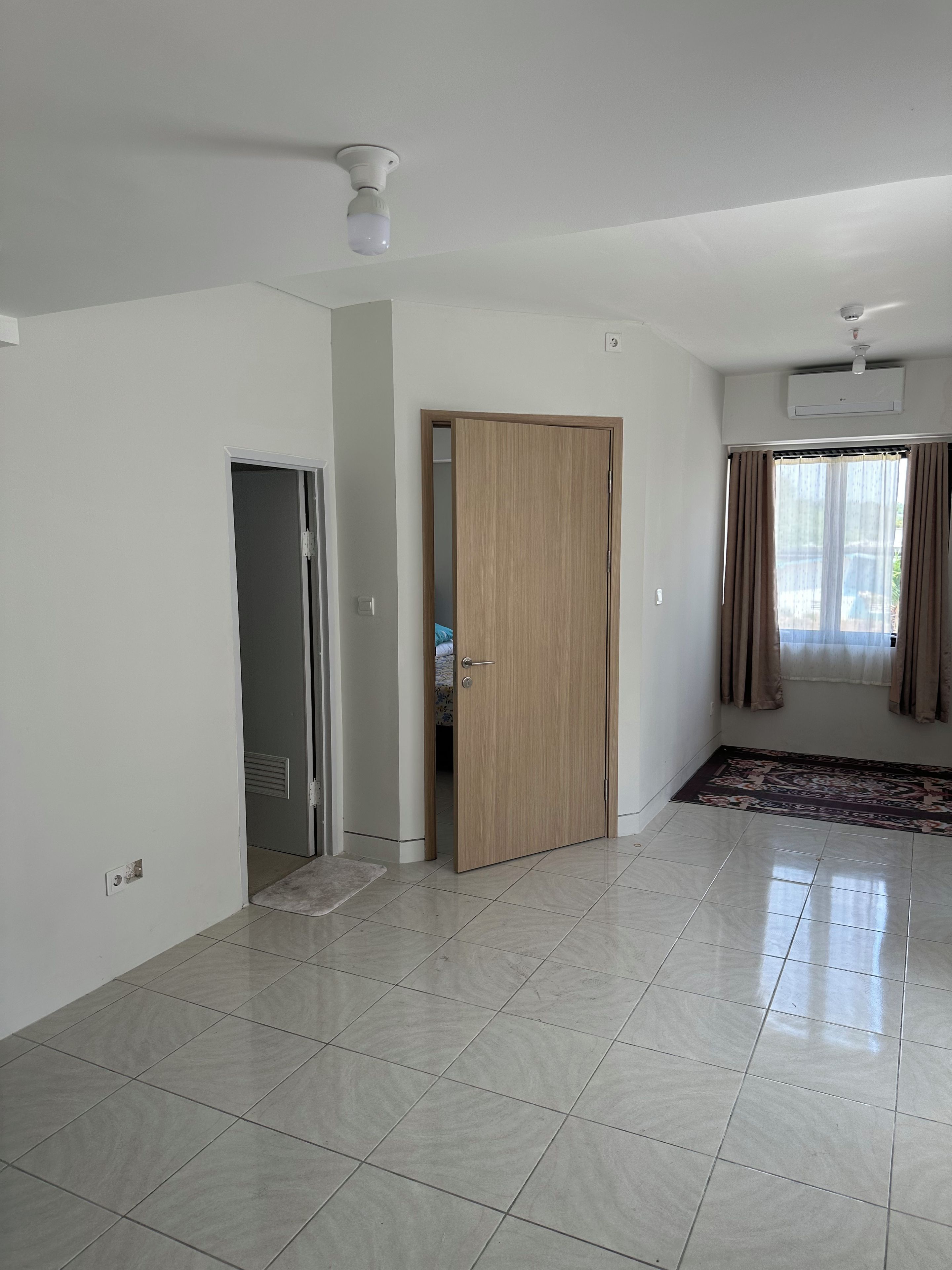 Quarto espaçoso com piso de azulejo, porta de madeira, janela com cortinas e ventilador de teto.