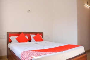 Cama com cabeceira de madeira, roupa de cama branca e detalhes em vermelho.