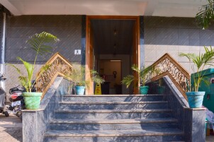 Entrada de edifício com degraus de mármore, corrimãos de metal e vasos de plantas.