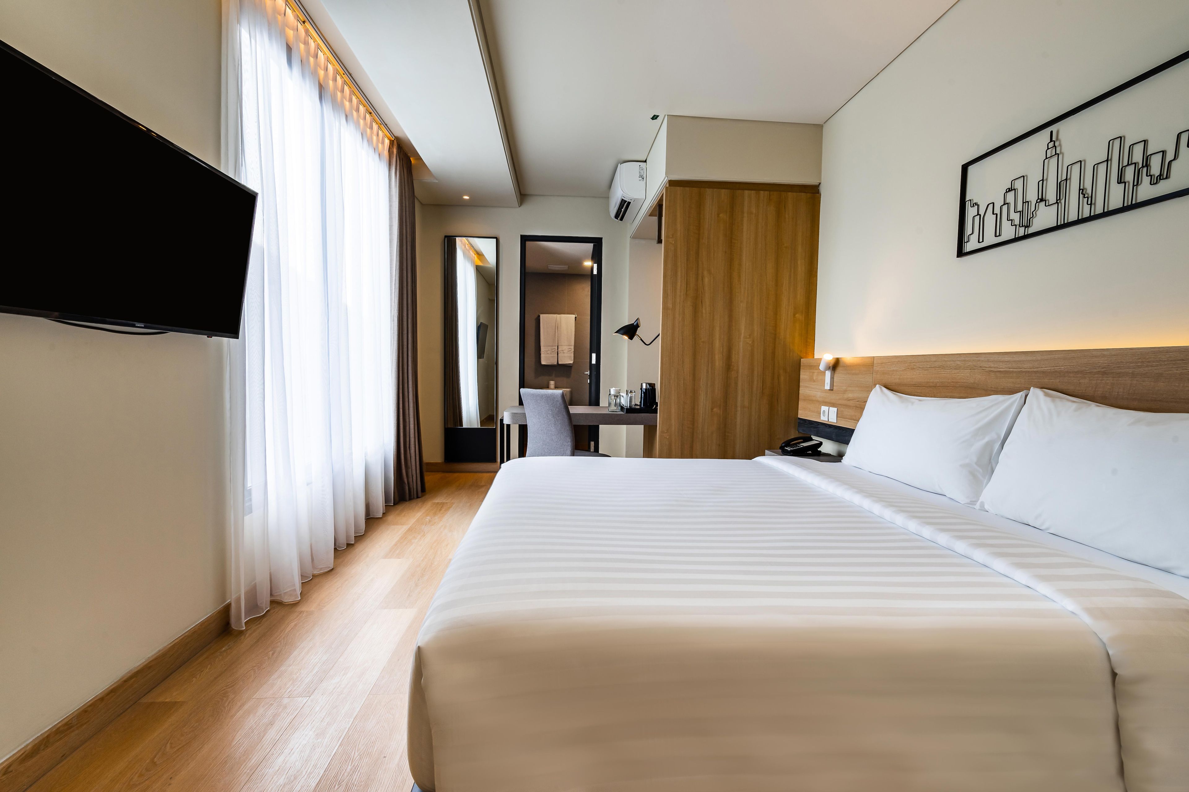 Quarto de hotel com cama grande, televisão de tela plana na parede, escrivaninha com cadeira e banheiro visível por uma porta aberta.