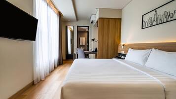 Quarto de hotel com cama grande, televisão de tela plana na parede, escrivaninha com cadeira e banheiro visível por uma porta aberta.