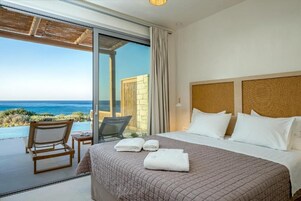 Quarto de hotel com cama, uma cadeira, uma mesa e vista para o oceano.