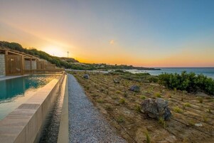 Piscina próxima a uma paisagem rochosa, com o pôr do sol ao fundo.