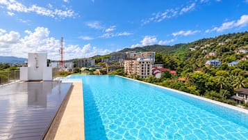 Piscina com deck de madeira, cercada por edifícios e uma paisagem montanhosa.